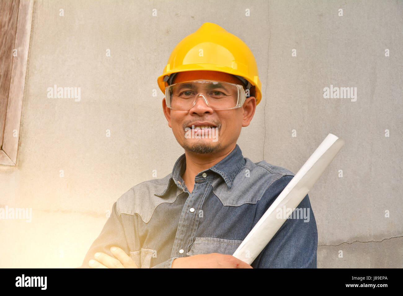 Portrait of confident architect man holding blueprints with yellow ...