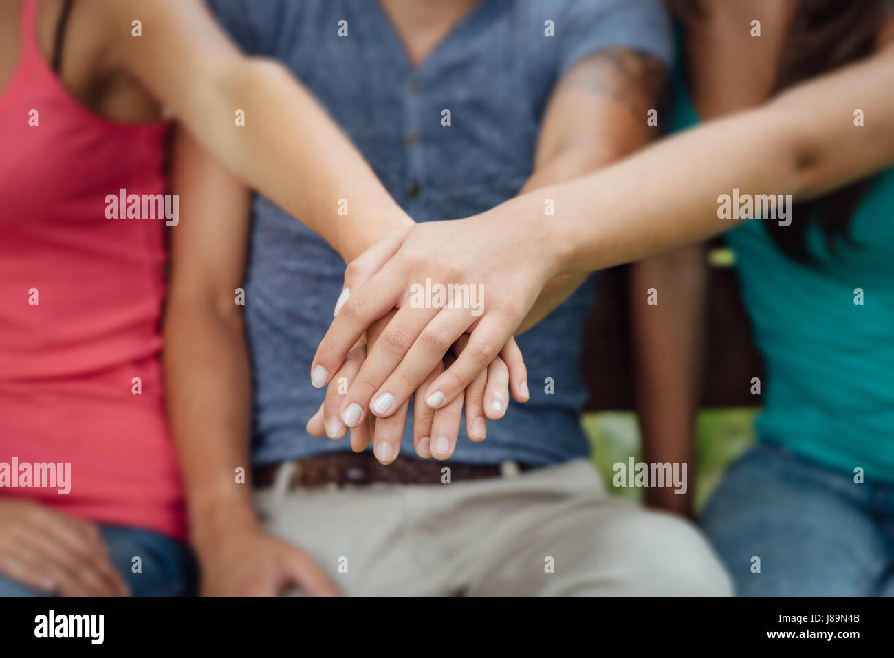 Young teenagers sitting on a wooden bench and stacking hands ...