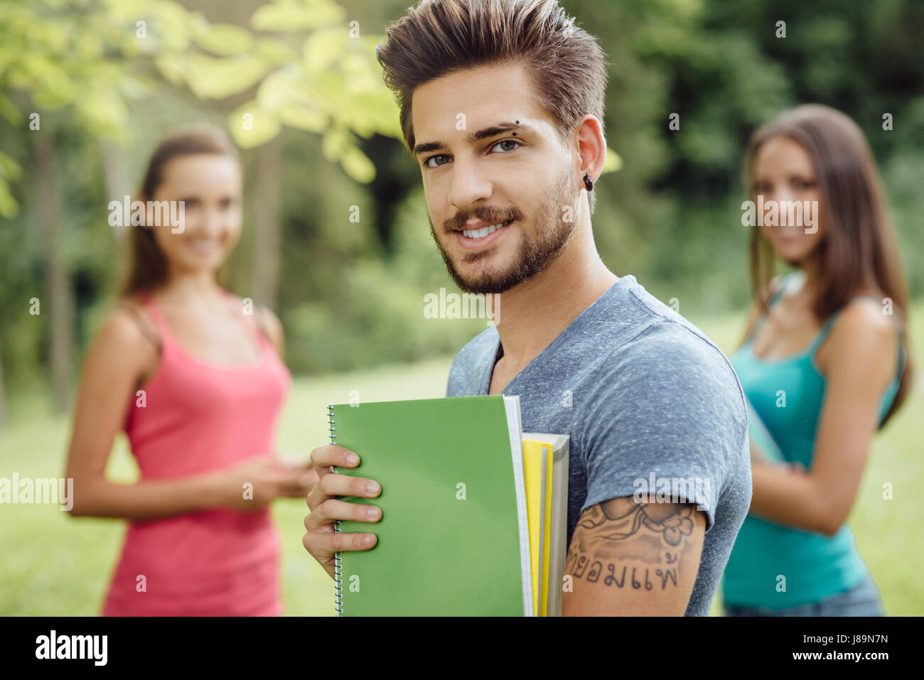 Handsome male young student with notebooks posing at the park and ...