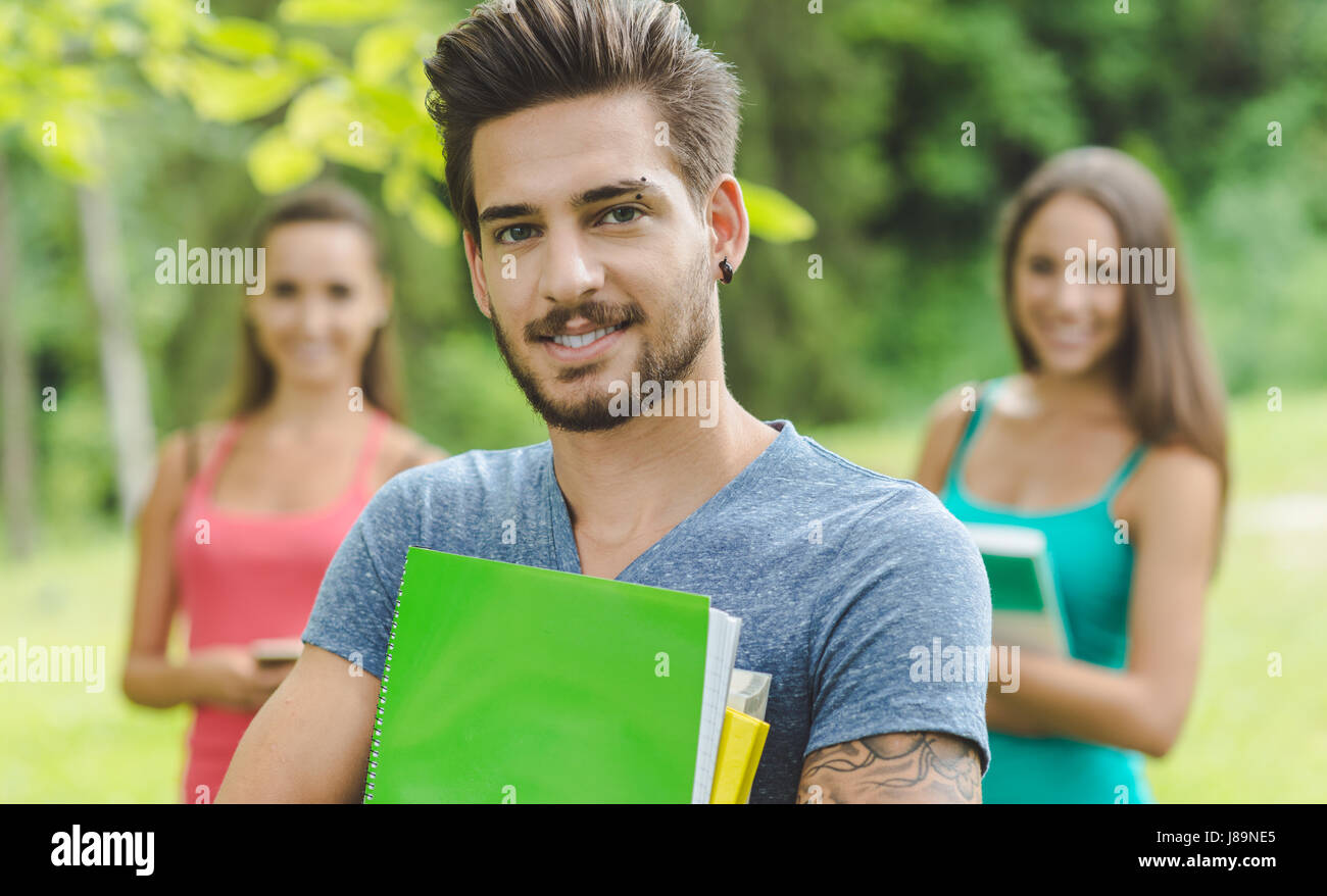 Handsome male young student with notebooks posing at the park and ...
