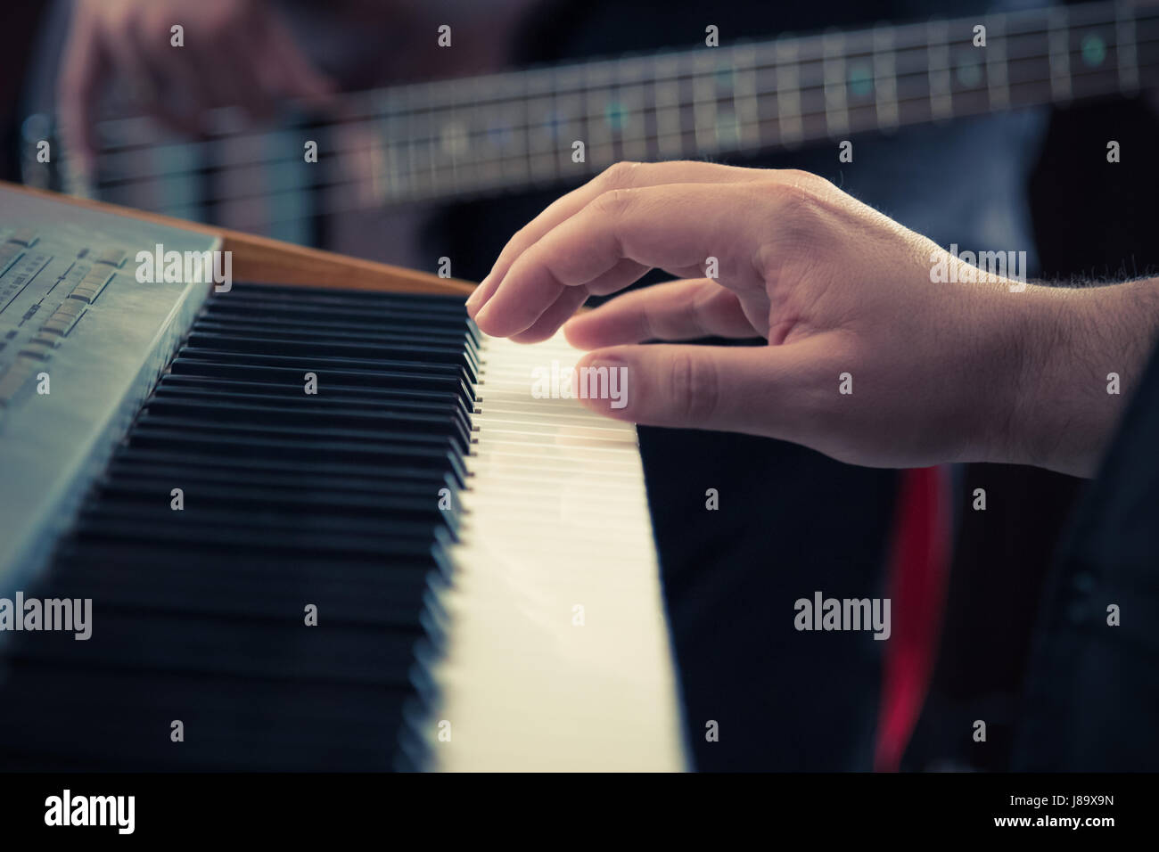 Hand playing music keyboard and bass guitar player in the background ...