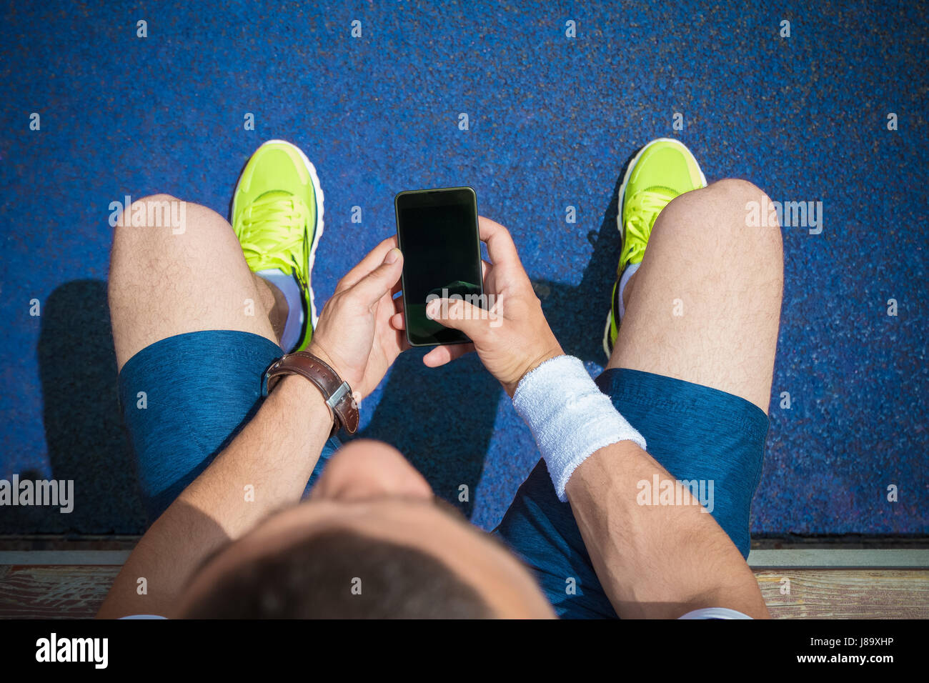 Jogger sitting on bench next to the blue jogging track and using ...