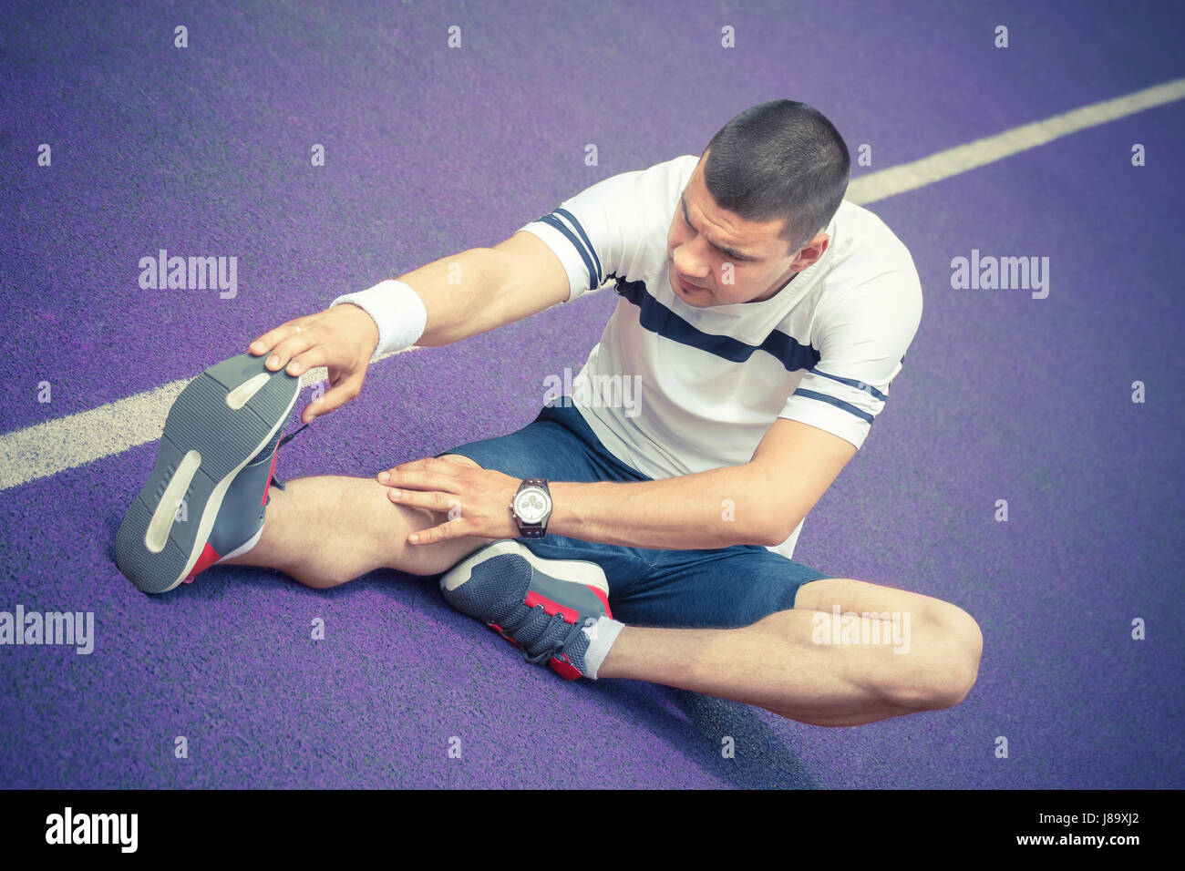Man stretching hamstring leg muscle on the purple running track while ...