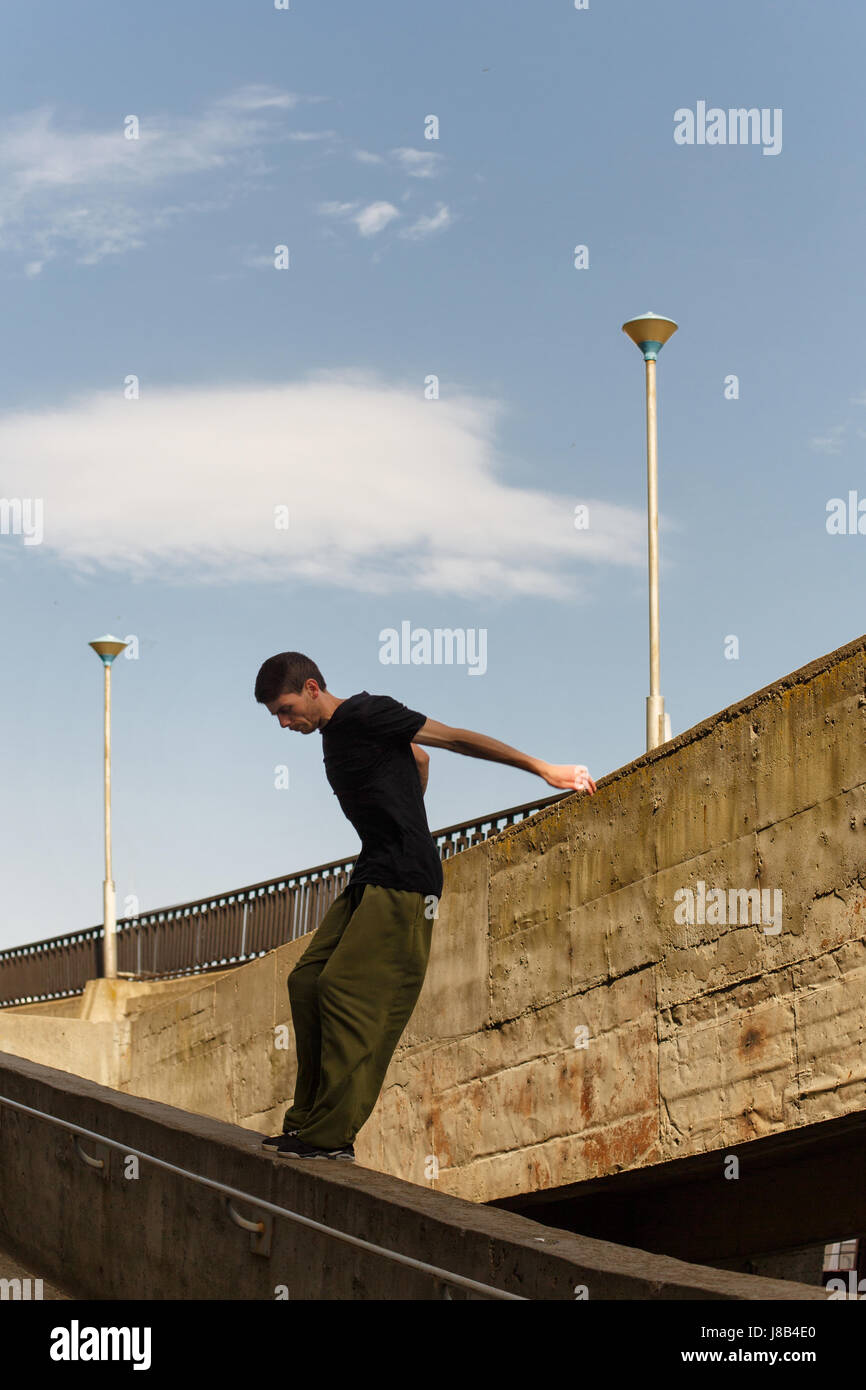 A young man is jumping from a high wall. Parkour in the urban space ...