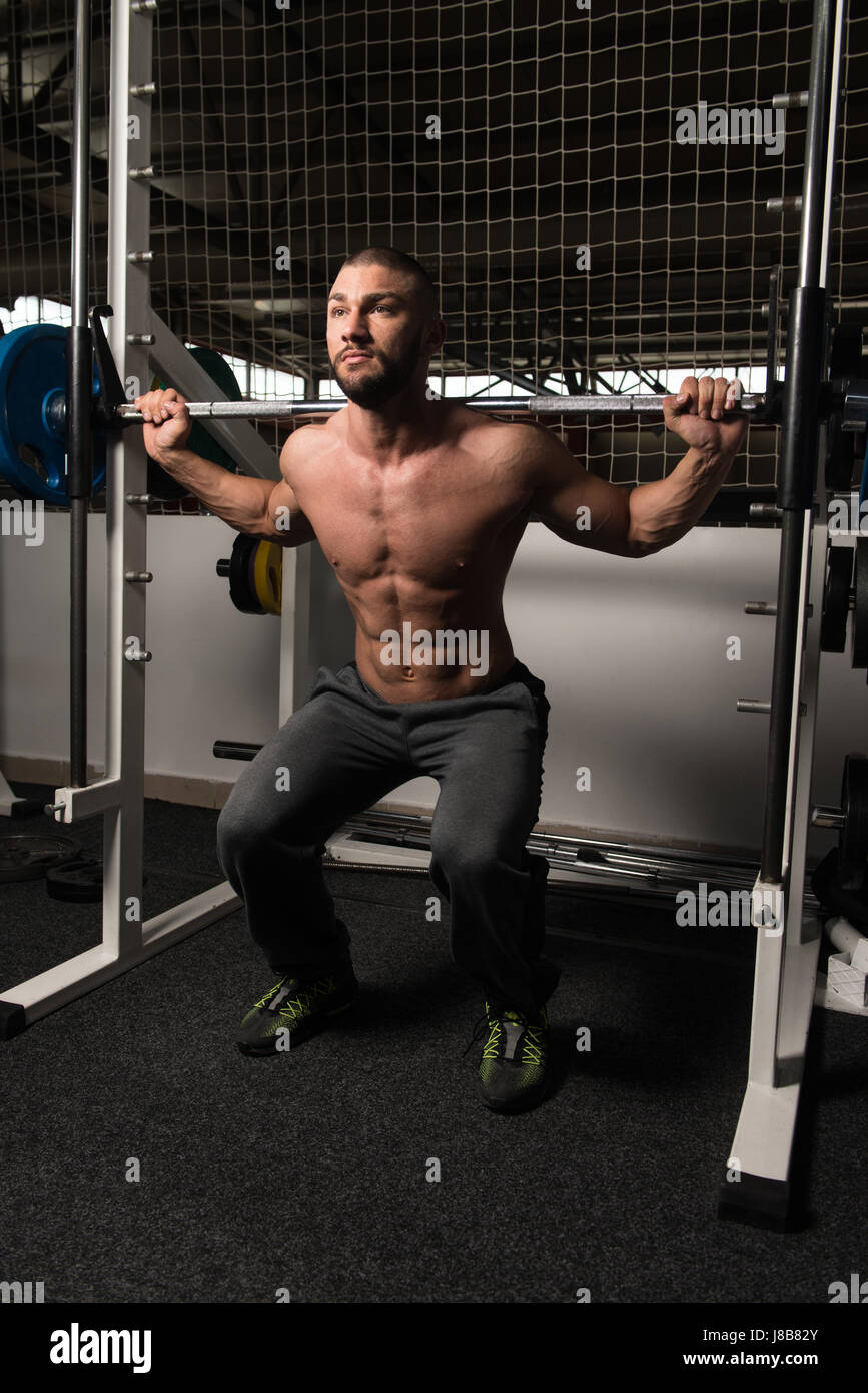 Healthy Fitness Man Working Out Legs With Barbell In A Gym - Squat ...