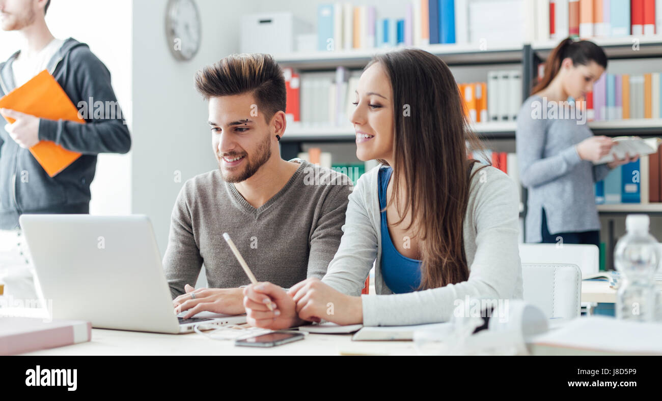 Smiling college students sitting at desk and studying together, they ...