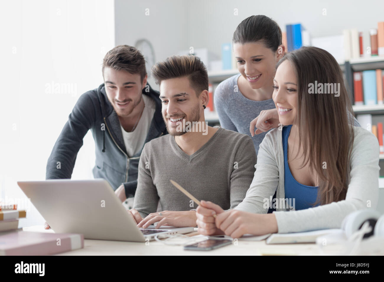 Group of smiling college students using a laptop and studying together ...