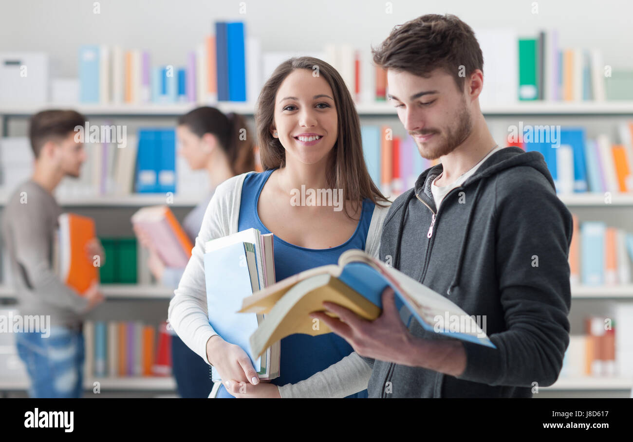 Happy smiling students in the school library, they are holding books ...