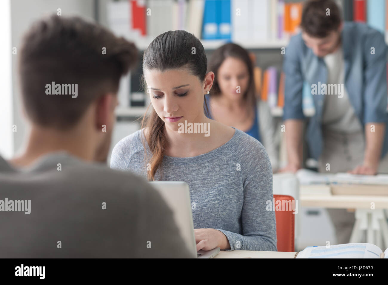 Young student girl sitting at the library desk and studying ...