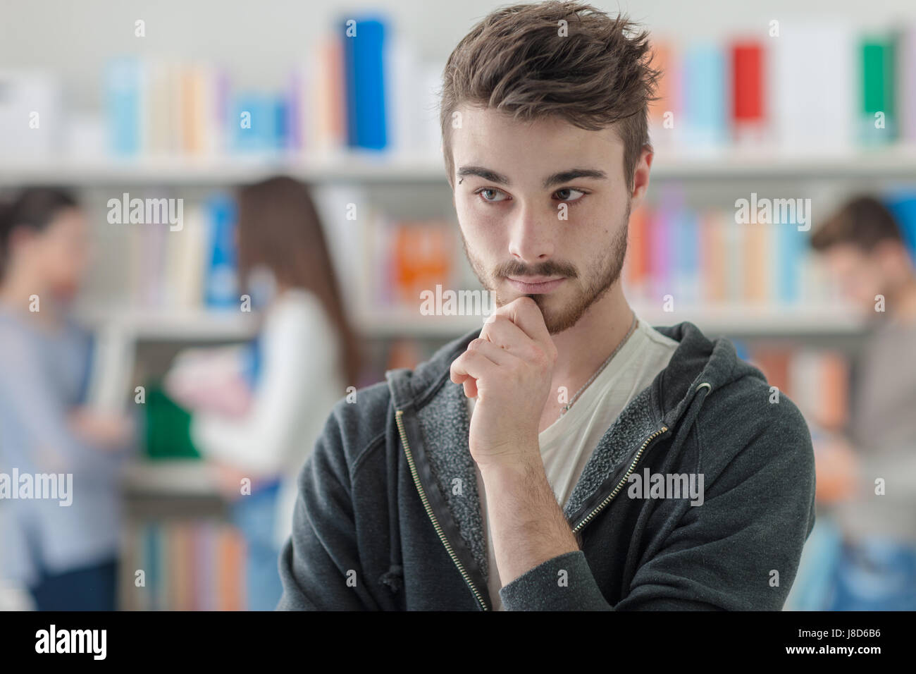 Confident handsome student posing in the library, he is thinking with ...