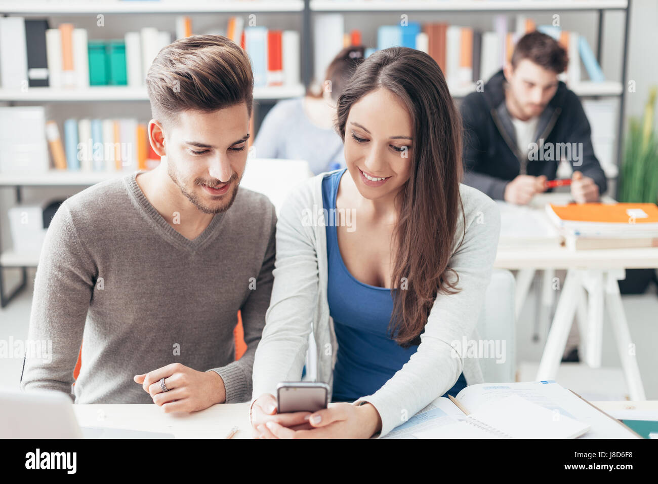 Smiling college students sitting at desk and studying together, they ...