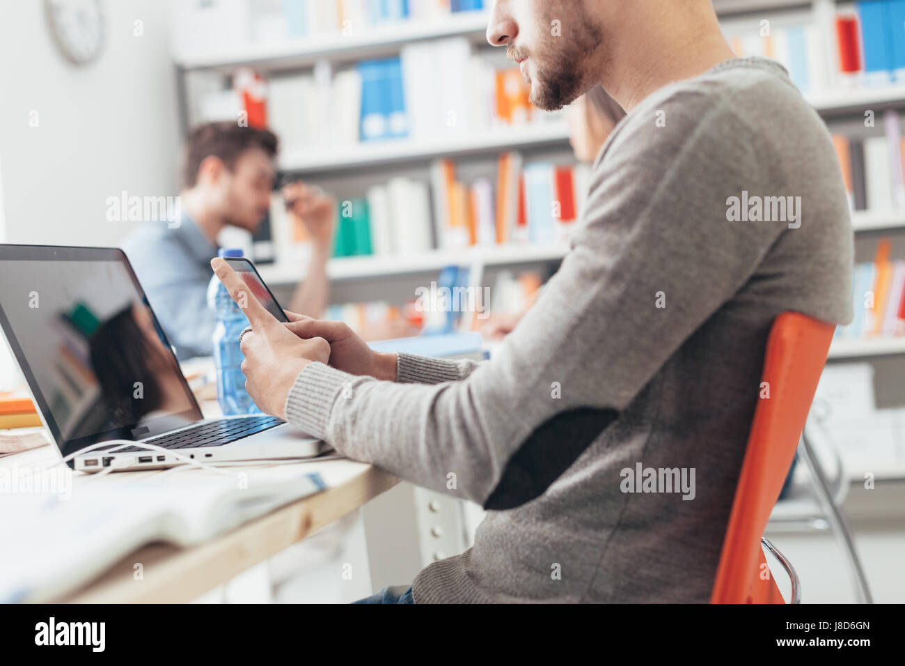 Young college student sitting at desk, using a touch screen smart phone ...