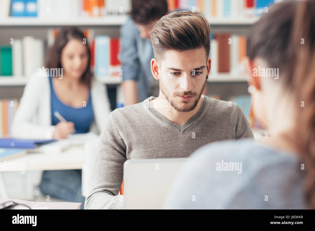 Male student sitting at desk and using a laptop, students and ...