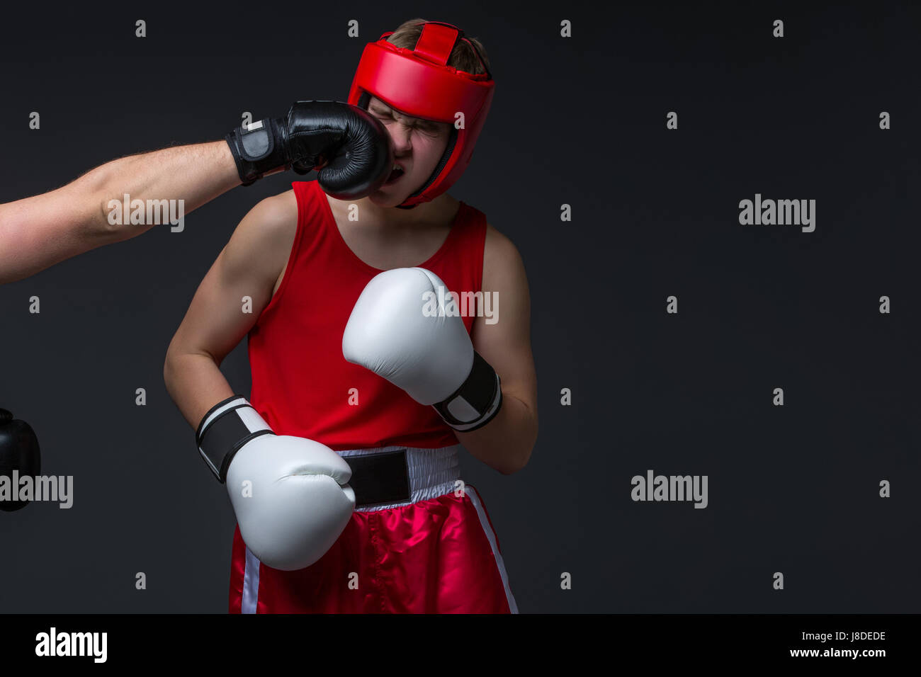 Teenage boxer in red form and helmet getting punched into face. Studio ...