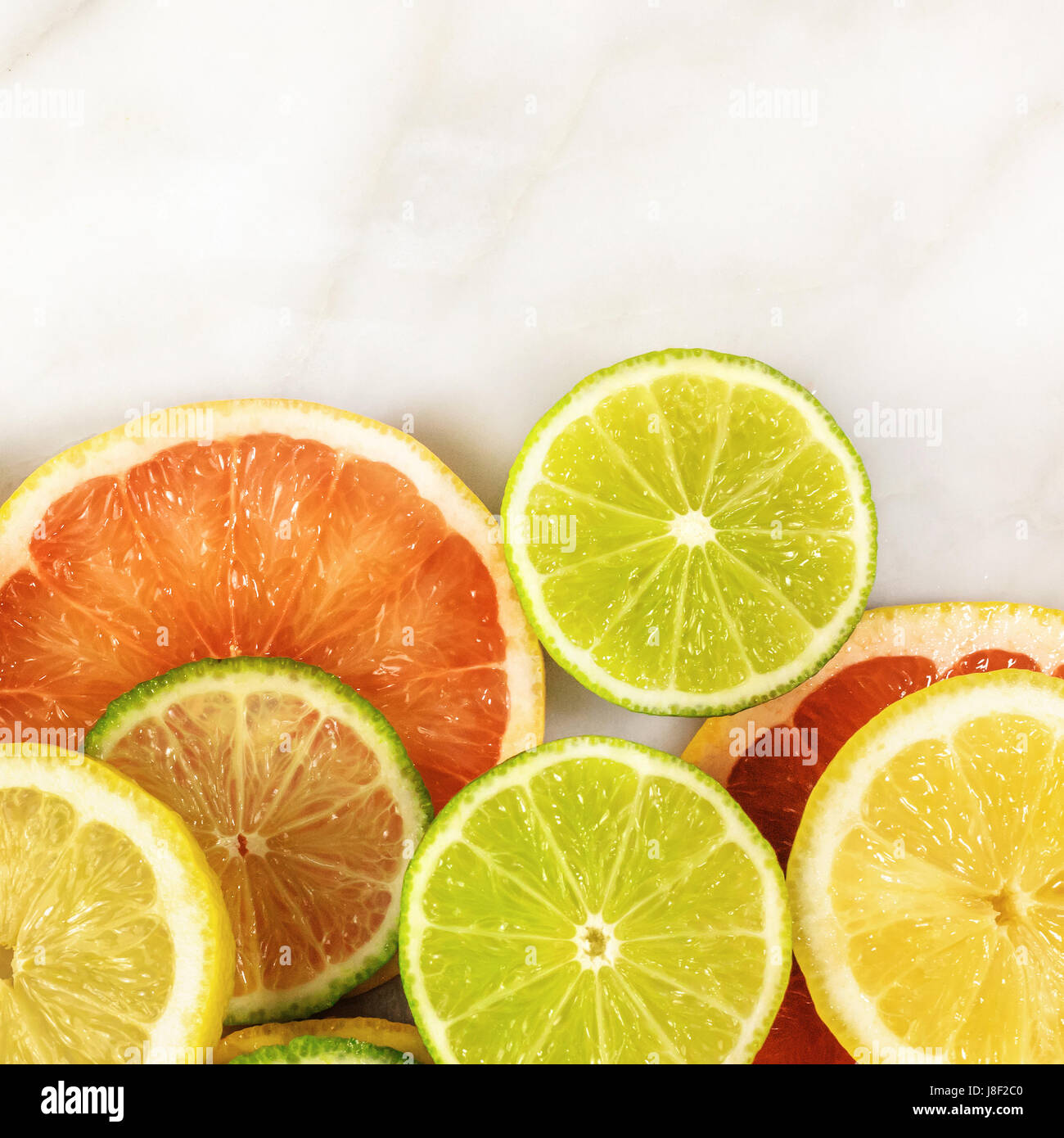 A square photo of vibrant juicy citrus fruits on a white marble texture ...