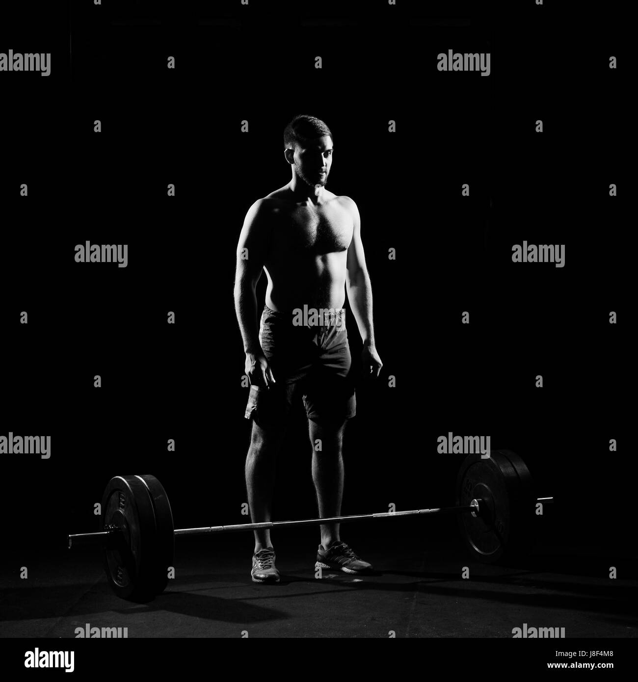 Fitness training. Man standing with barbell in dark gym Stock Photo - Alamy