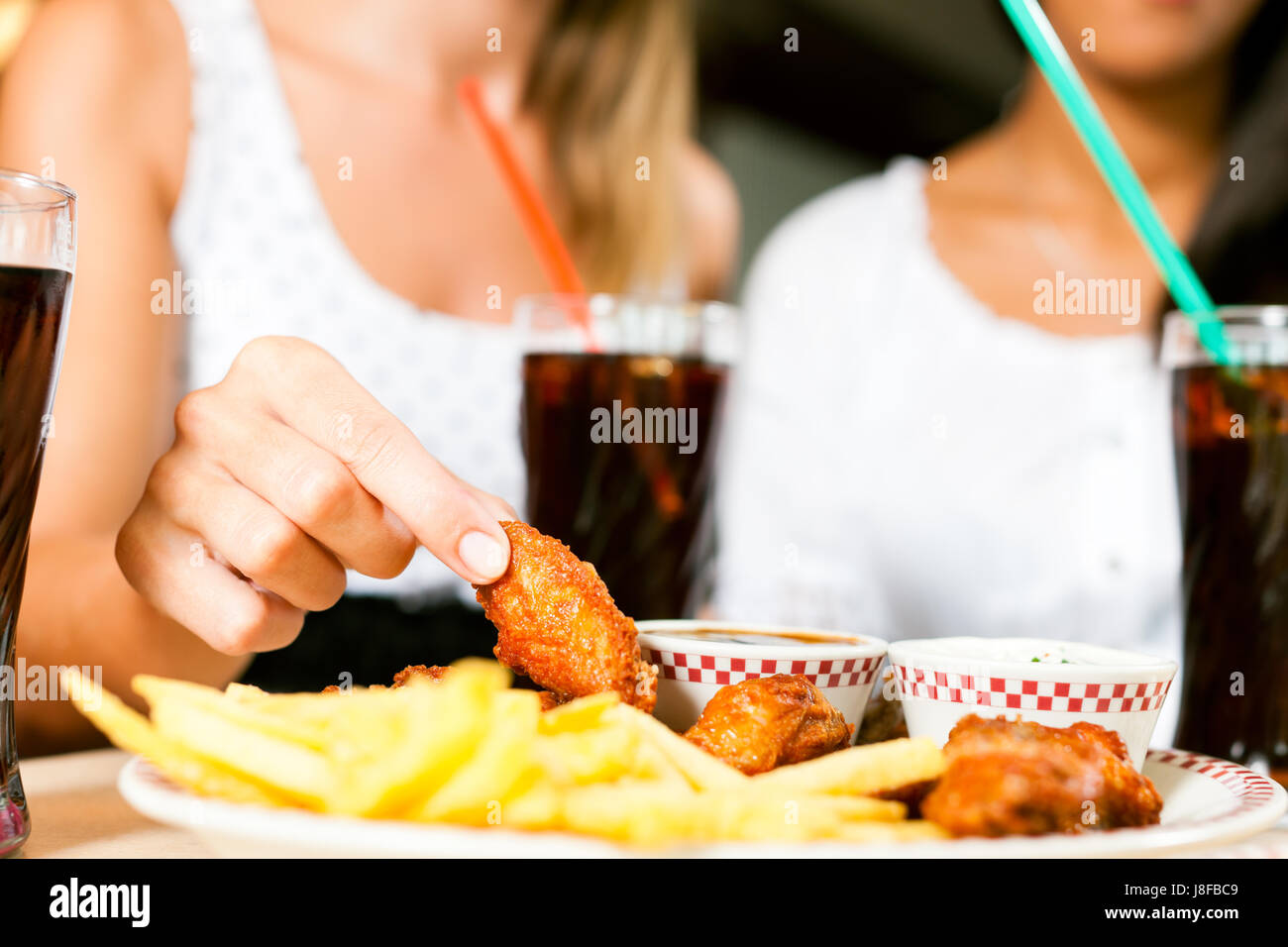 two women eating chicken wings and drinking cola Stock Photo - Alamy