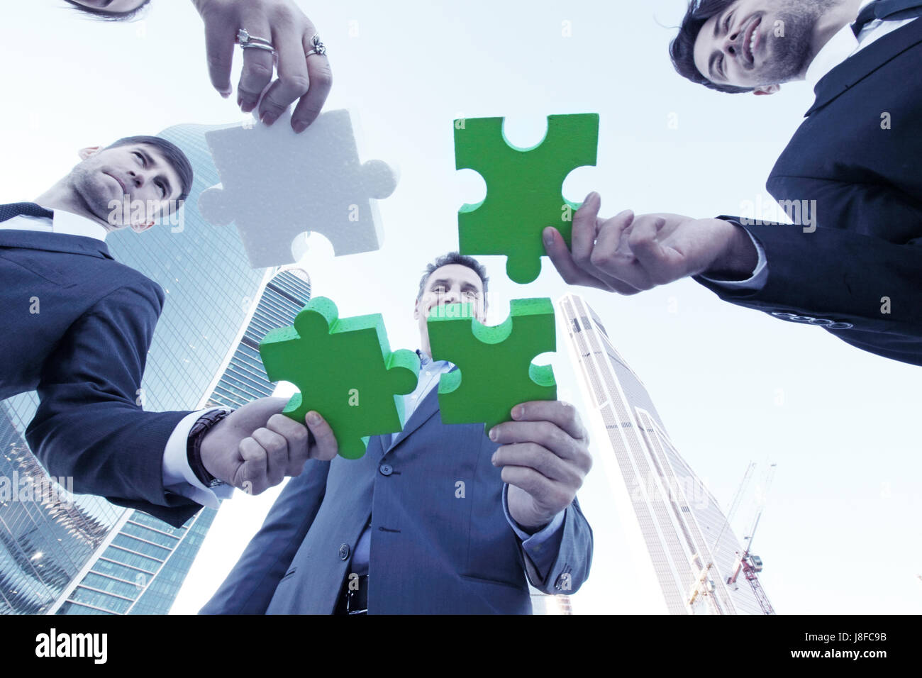 Business people assembling jigsaw puzzle near skyscrapers Stock Photo ...