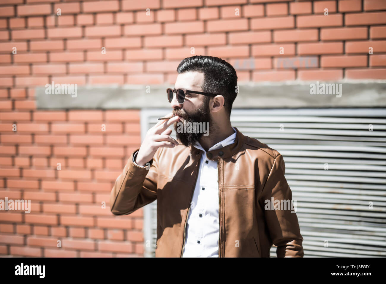 Brutal caucasian serious unshaven hipster smoking cigar on brick wall ...