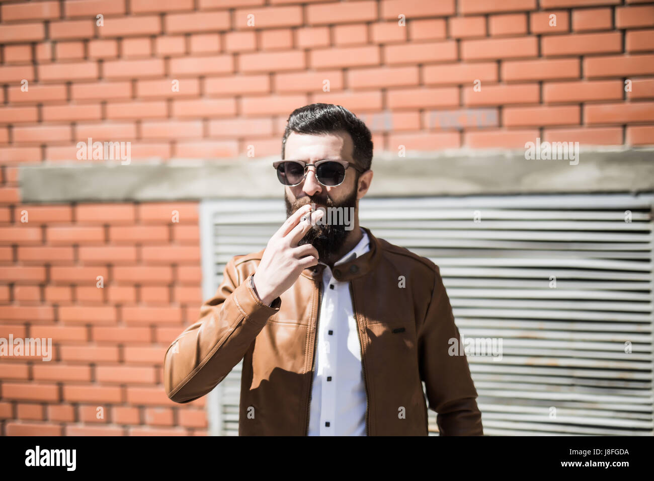 Brutal caucasian serious unshaven hipster smoking cigar on brick wall ...