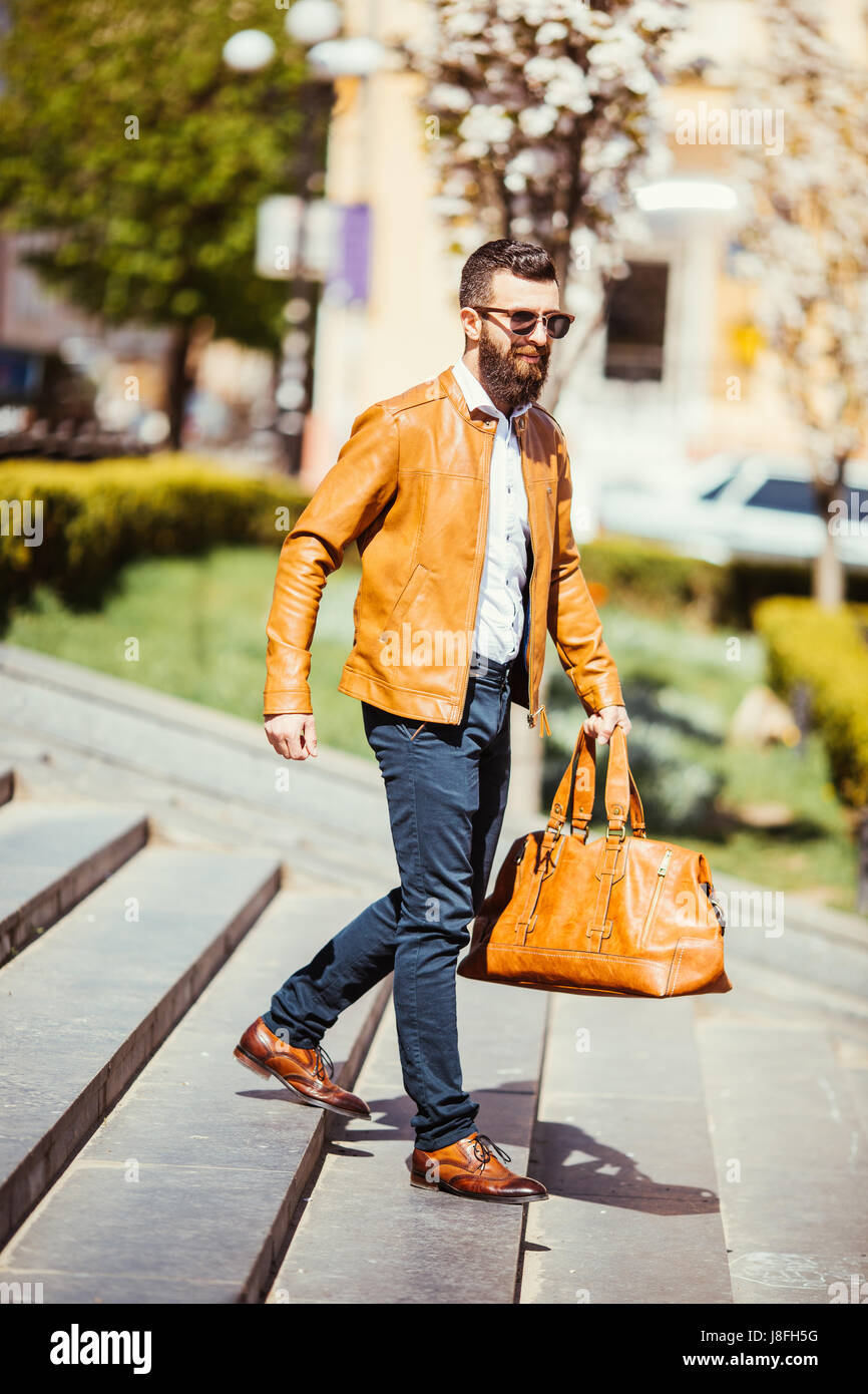 Handsome bearded man walking down on the stairs with bag on city ...
