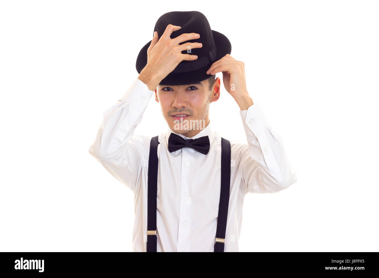 Elegant young man in white shirt with black bow-tie, suspenders and hat ...