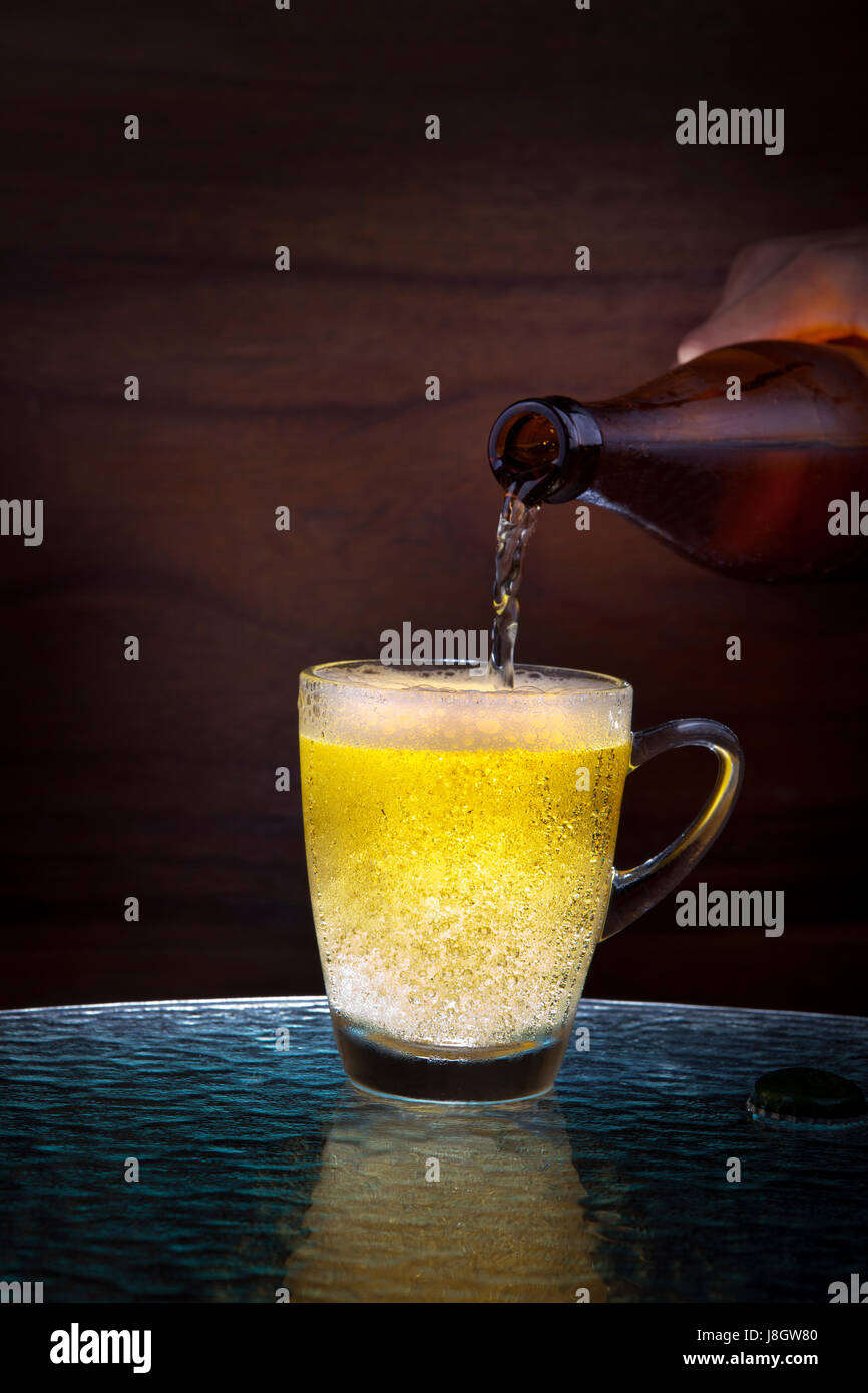 lager beer drain from bottle to glass on table with wood backgrond ...