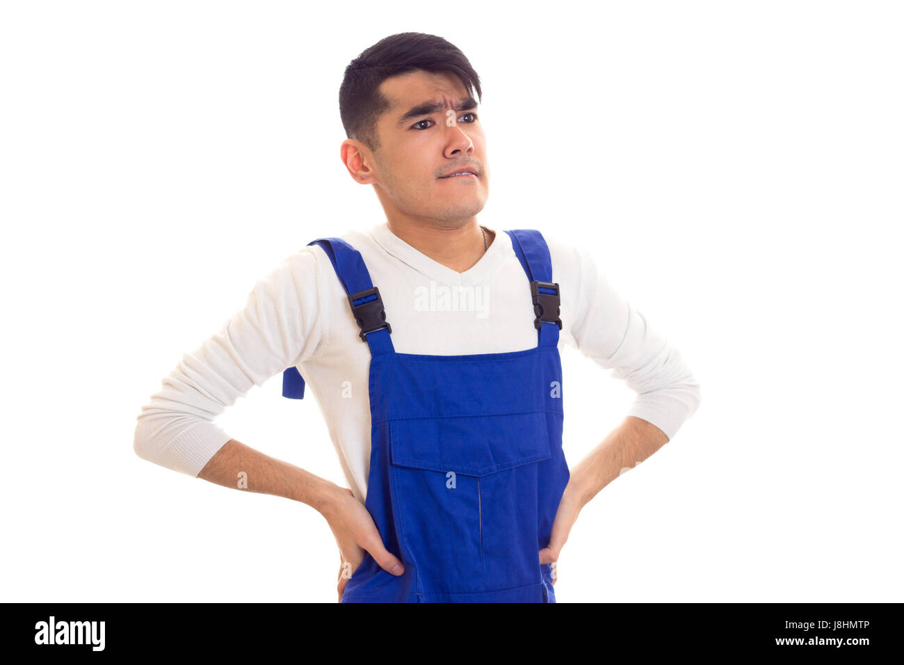 Angry young man with dark hair wearing in white shirt and blue overall ...