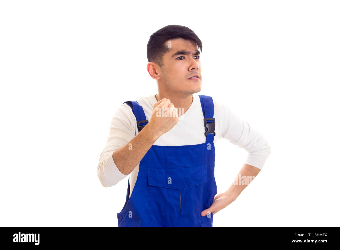 Young angry man with dark hair wearing in white shirt and blue overall ...