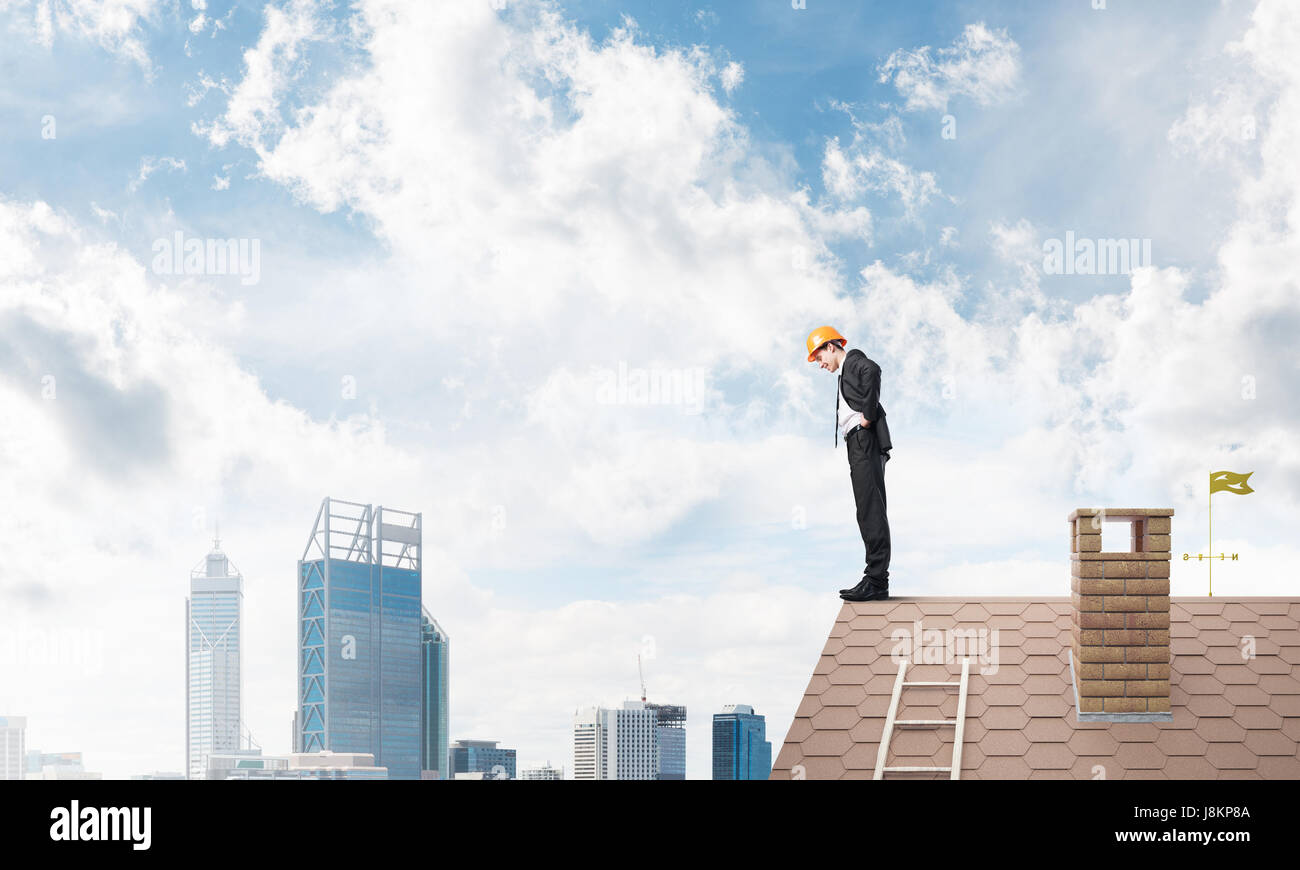 Businessman looking down from roof and modern cityscape at background ...
