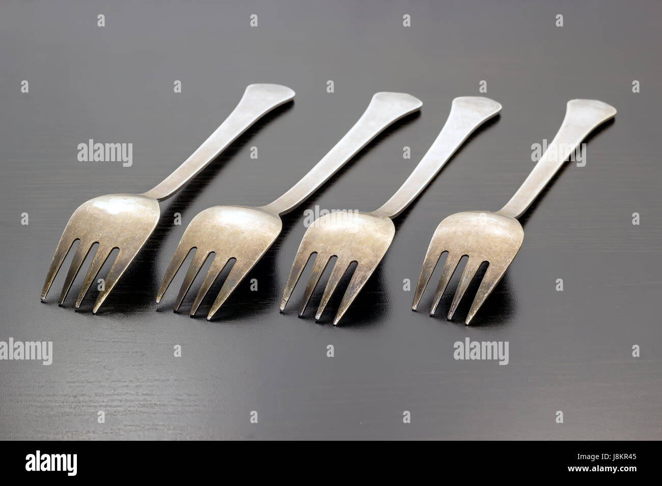 Four beautiful, silver forks lie on the blackened polished wooden ...