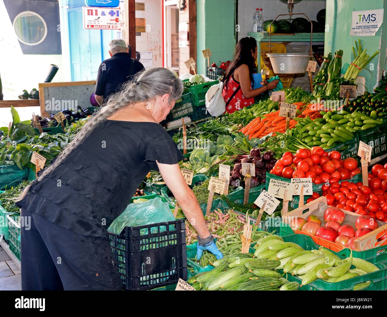 Cretan stallholder sorting vegetables on a market stall in the city ...