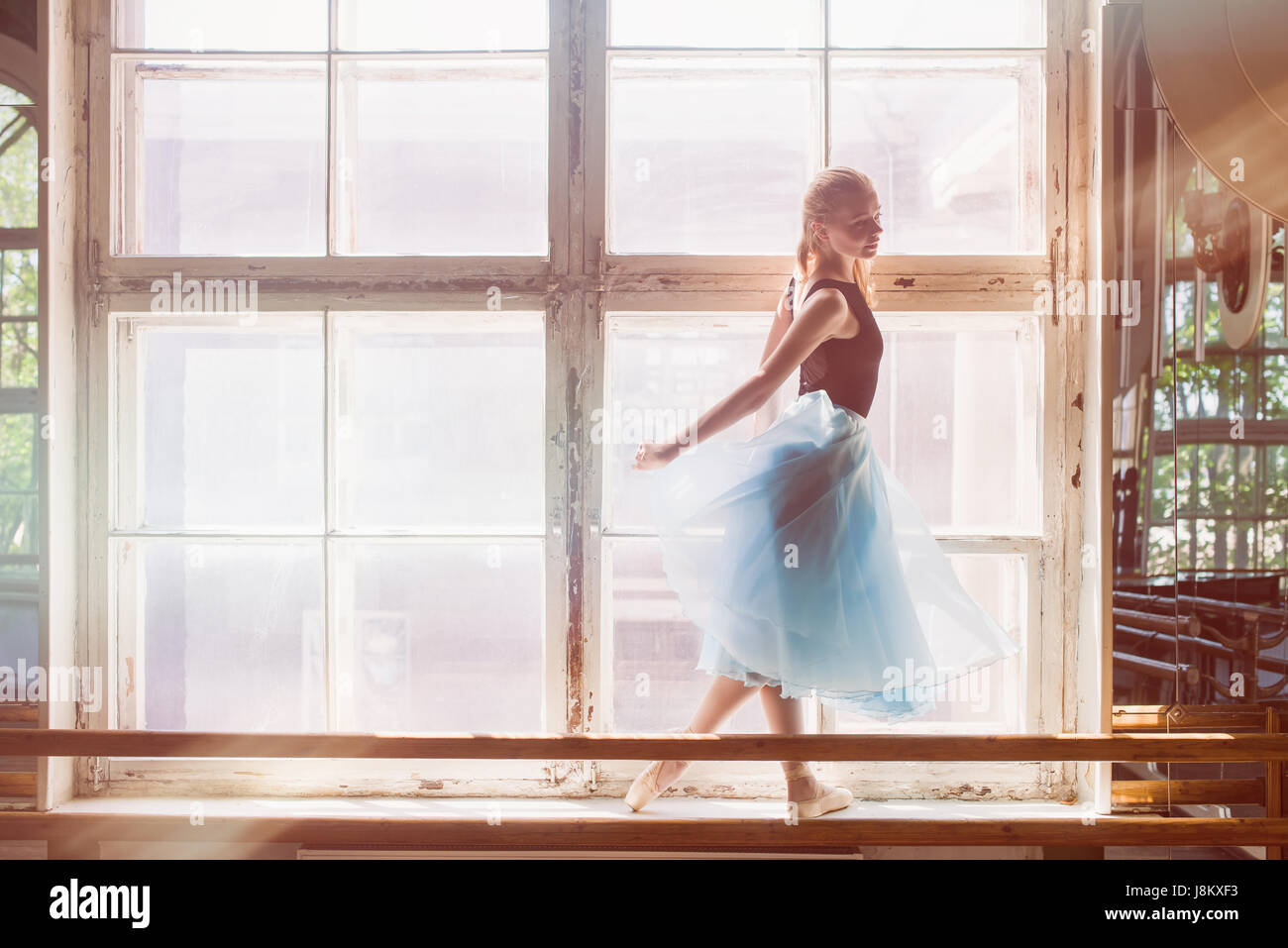 A ballerina is dancing in front of a large window, standing on the ...