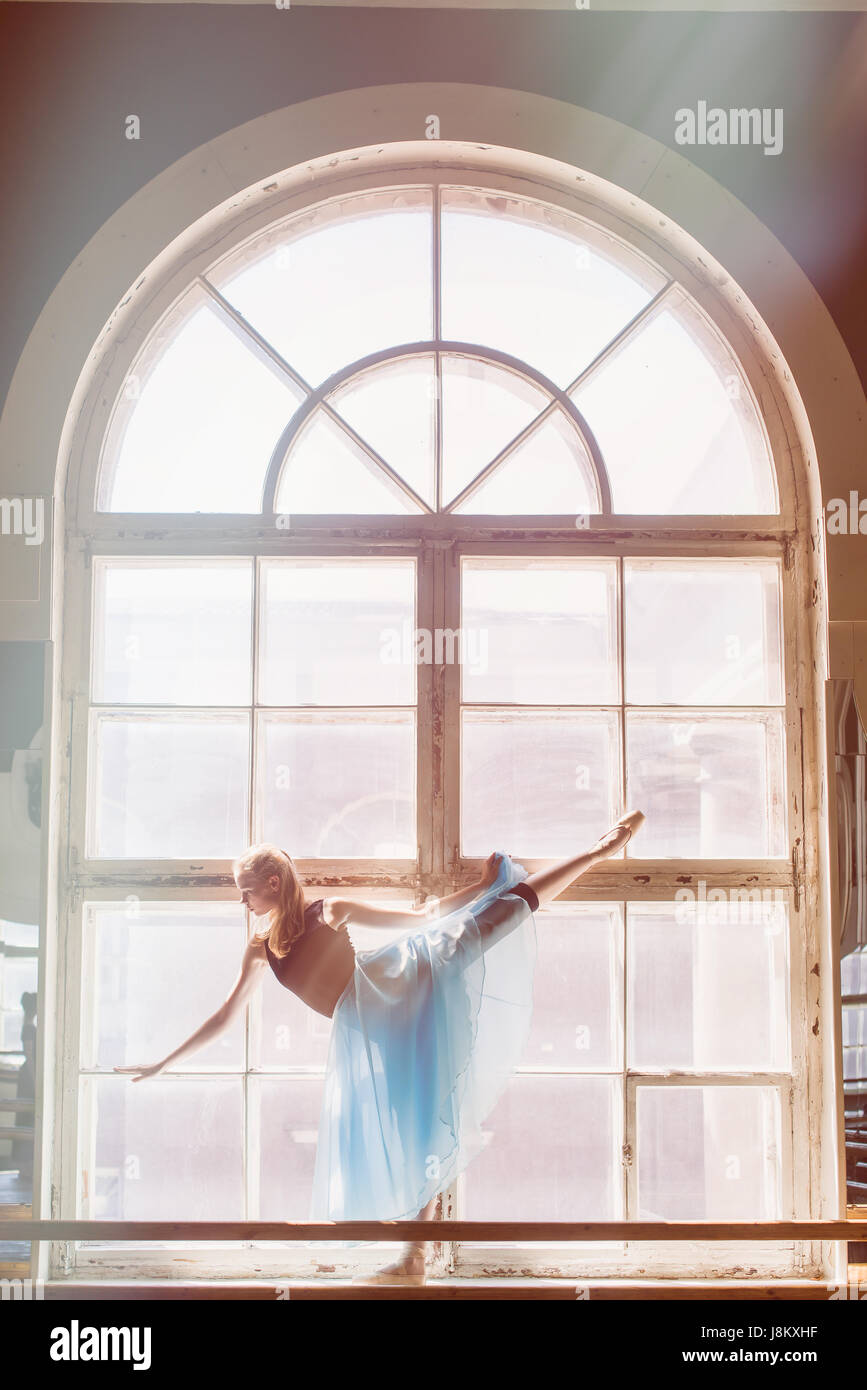 A ballerina is dancing in front of a large window, standing on the ...