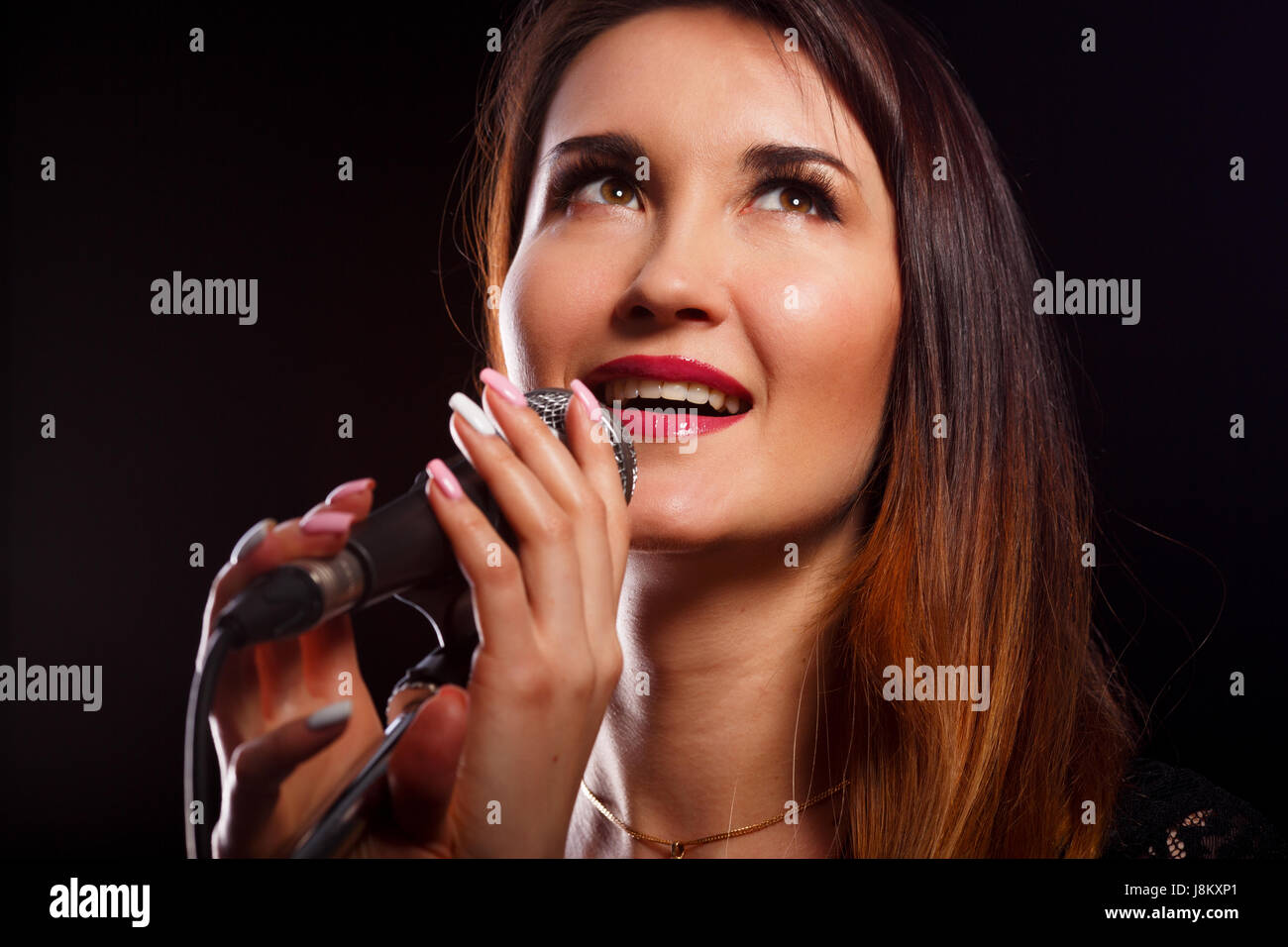 Singing woman with microphone on empty black background Stock Photo - Alamy
