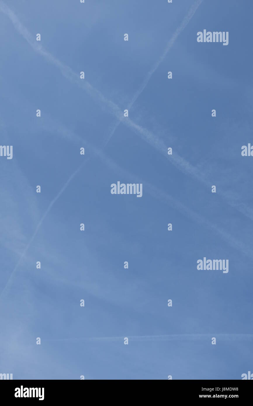 Jet trails, known as chemtrails or contrails over blue sky background ...