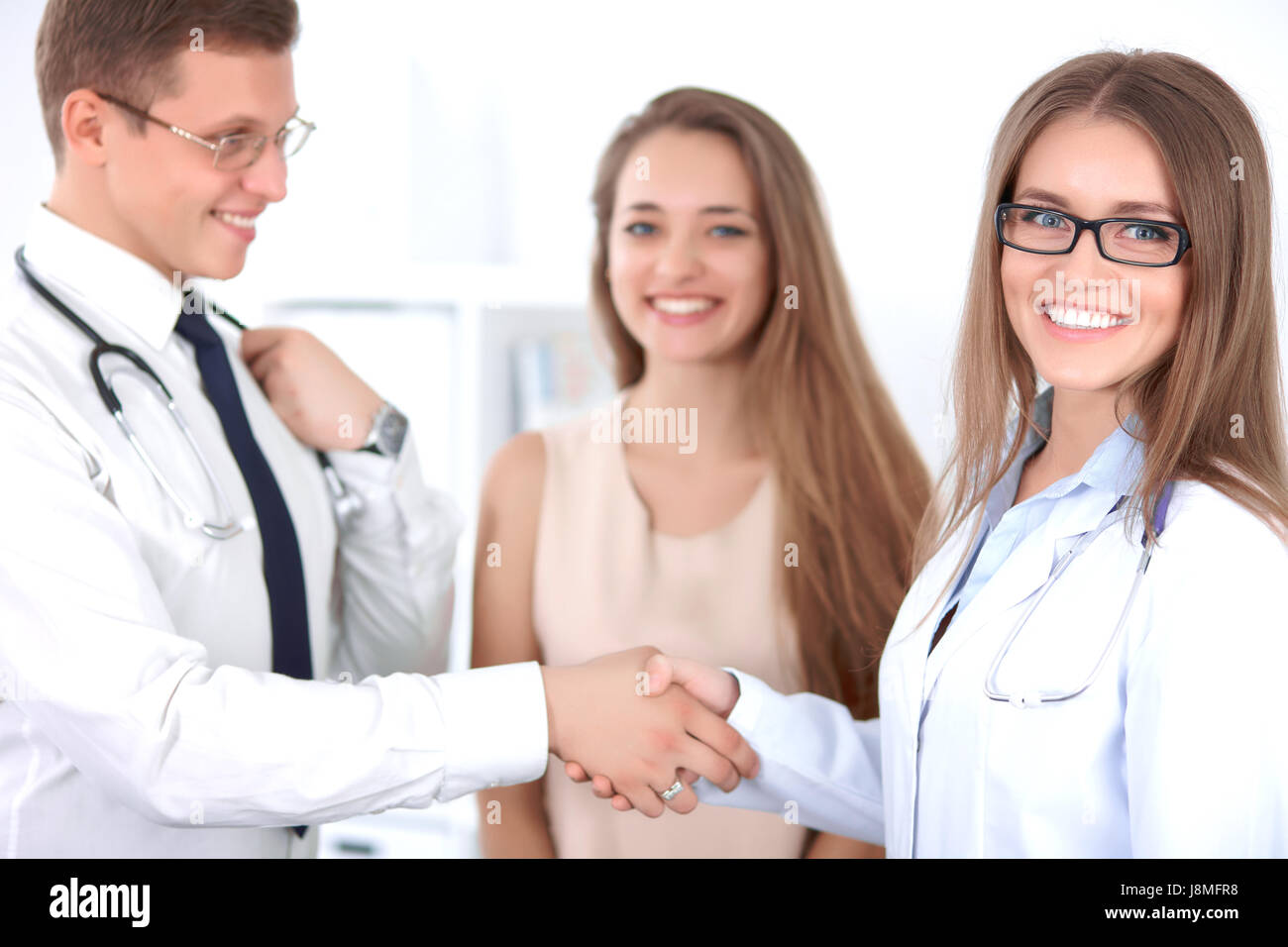 Two doctors shaking hands to each other while patient standing near ...