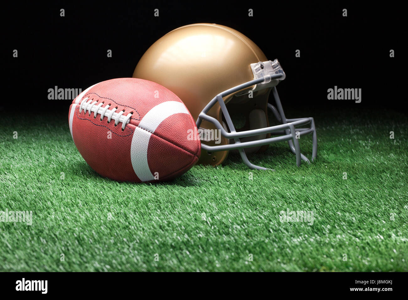 College style football and helmet on grass field against dark ...