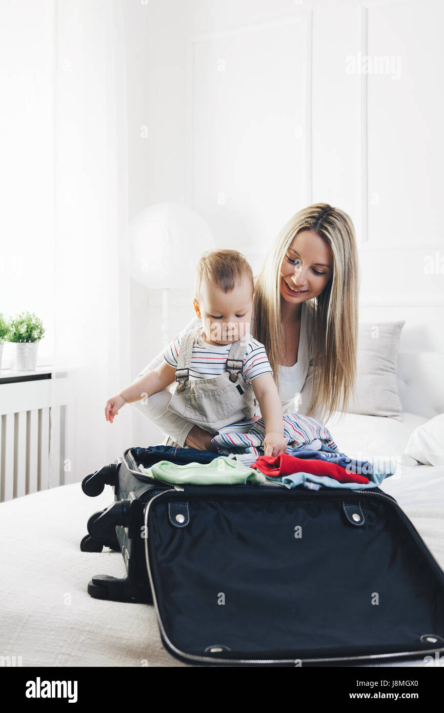 Travelling with kids. Happy mother with her child packing clothes for ...