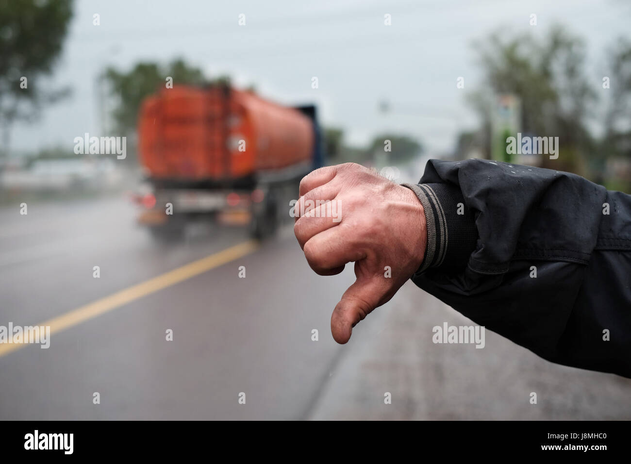 A male hand hitching a lift and a motorway with truck in the blurred ...