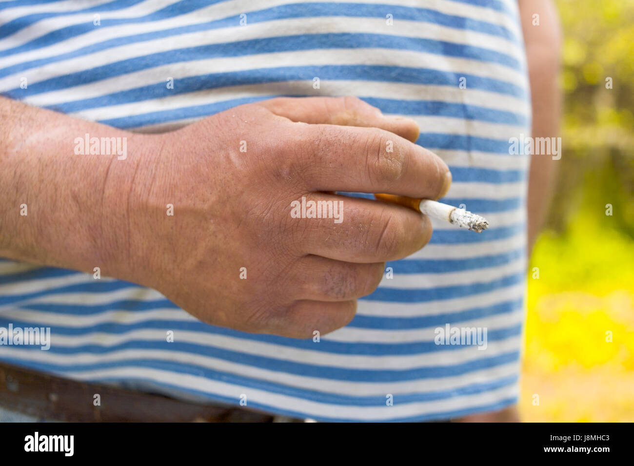 A smoker hand with unhealthy skin holding a cigarette, outdoor cropped ...