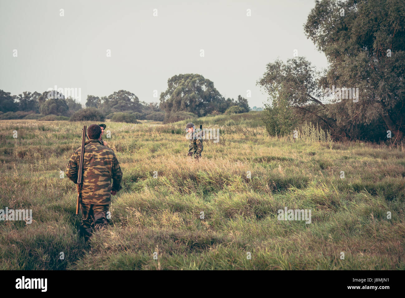 Hunters crossing through tall grass in rural field during hunting ...