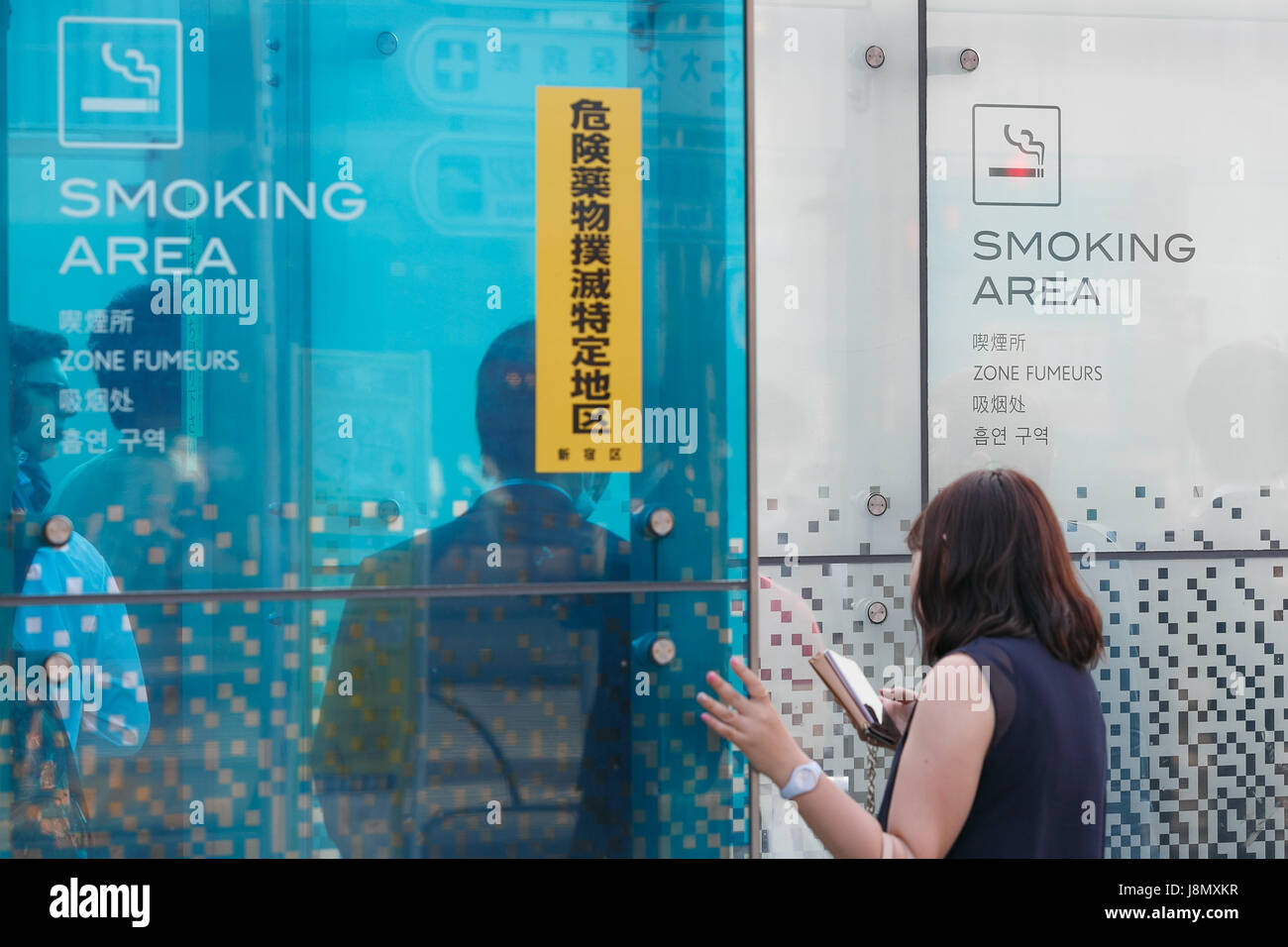 People smoke in a designated smoking area outside Shinjuku Station on ...