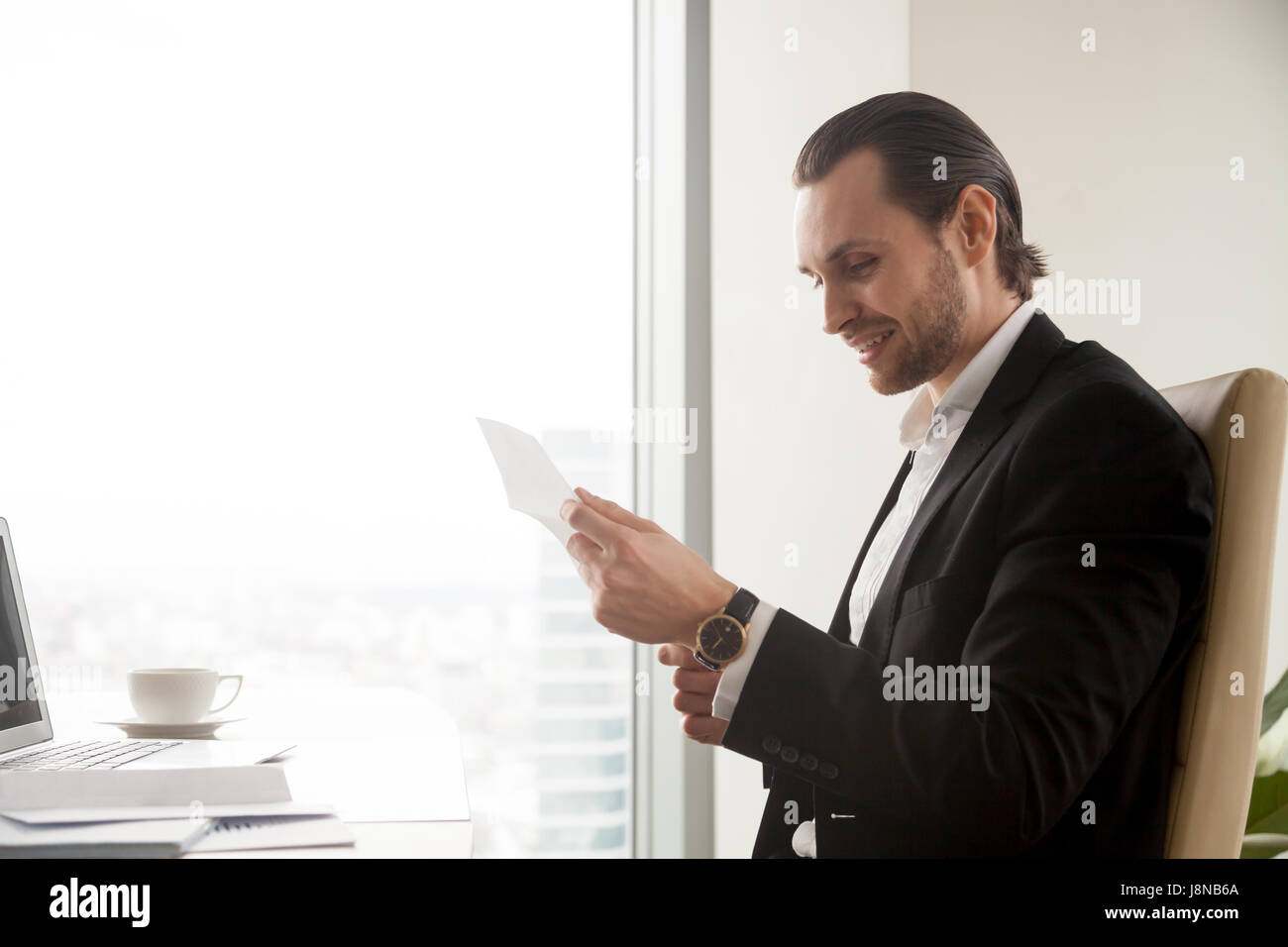 Happy businessman reading document at desk in office. Young guy ...