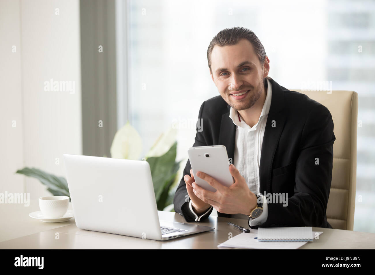 Successful businessman at desk with laptop using computer tablet ...