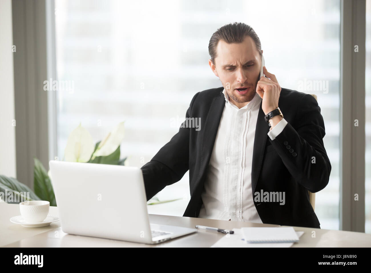 Angry businessman talking on the cellphone at work desk in office ...