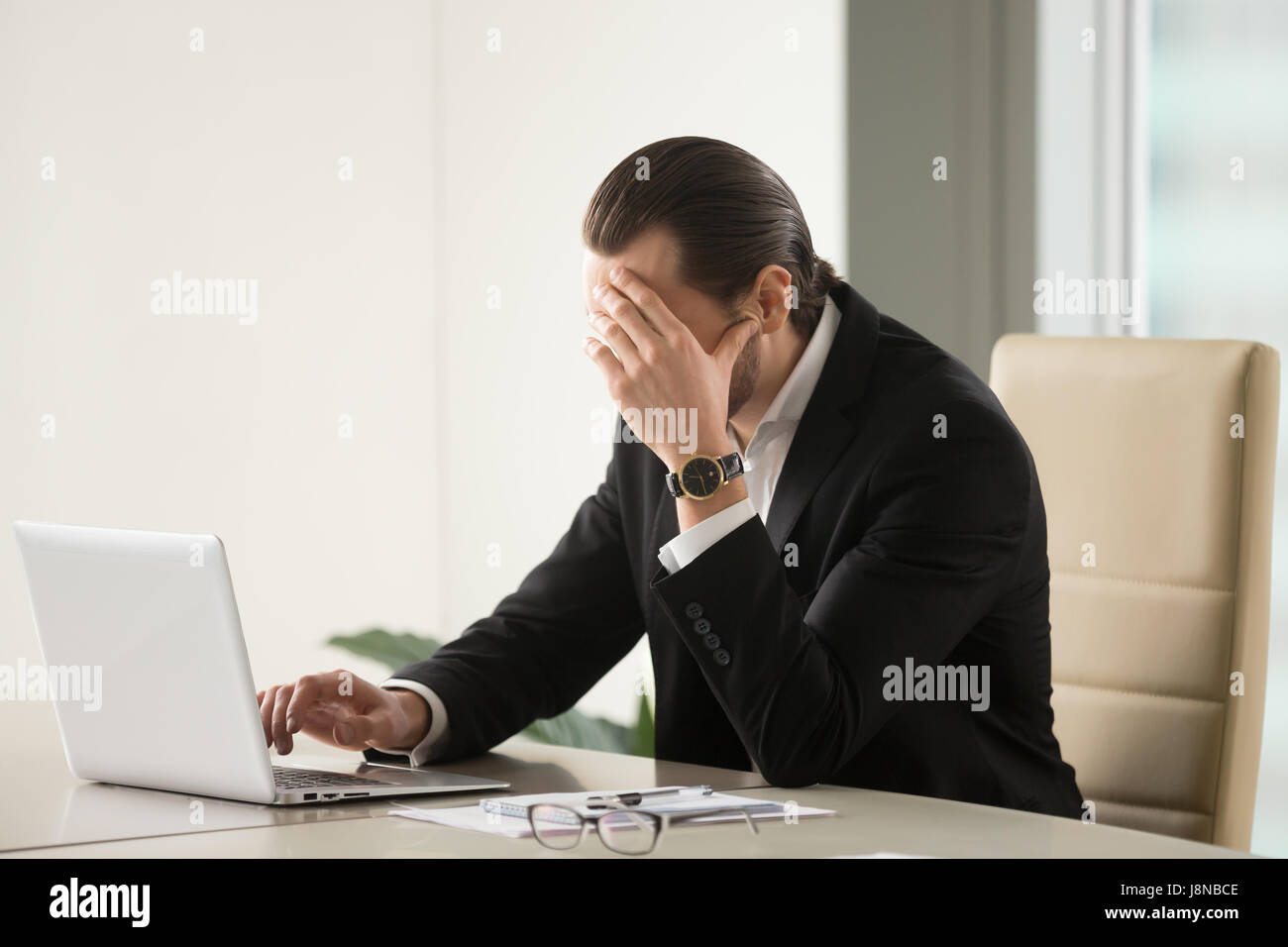Tired businessman at desk with laptop searching way out from difficult ...