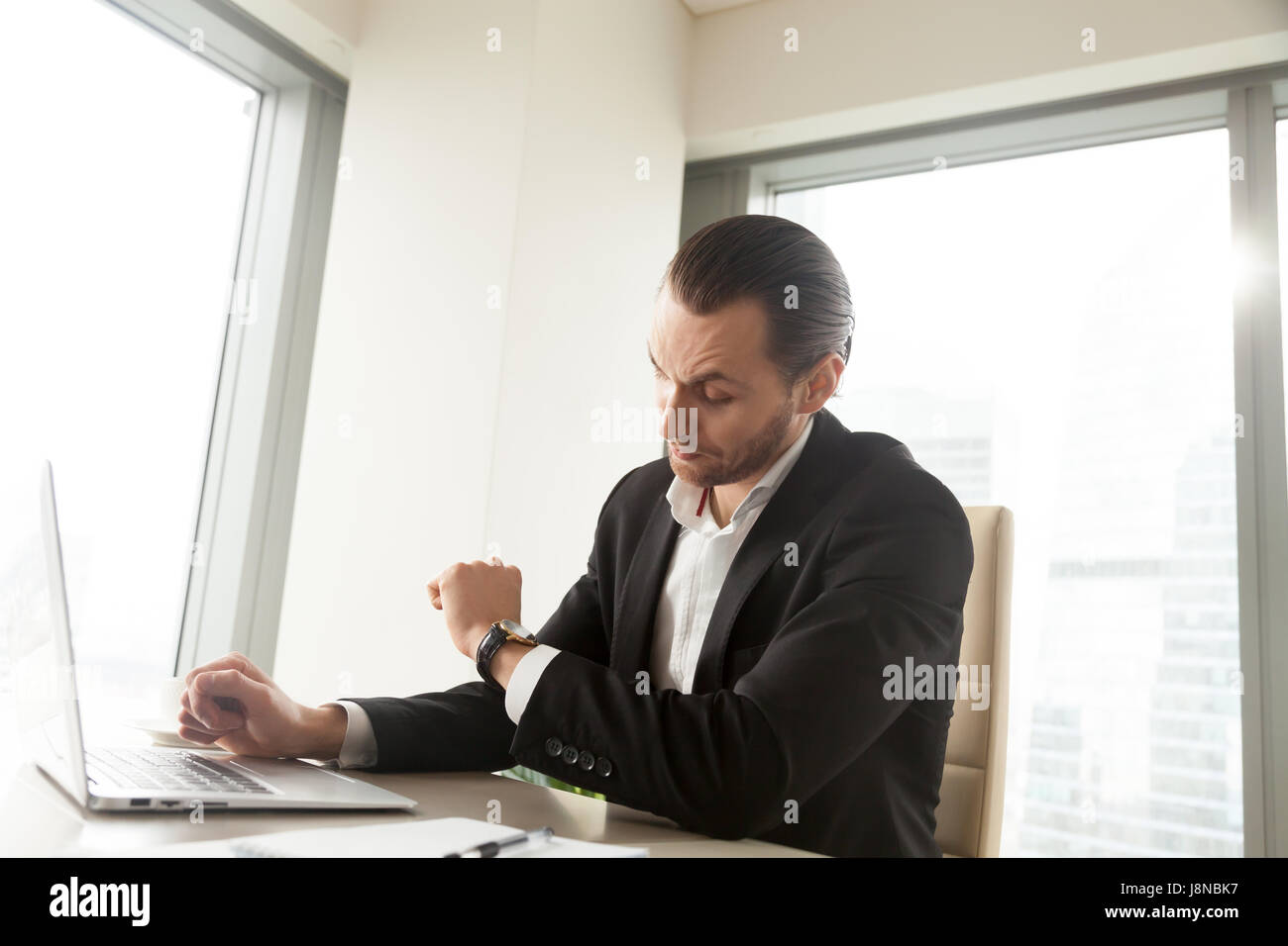 Office worker at desk looking at wristwatch, waiting for the end of ...