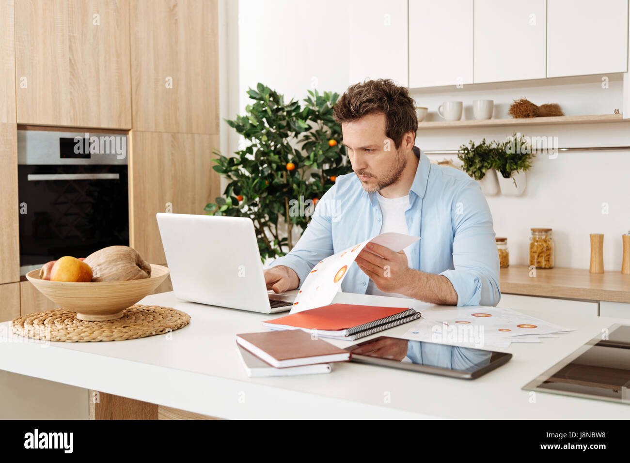 Busy day. Serious concentrated bristled man sitting in a modern kitchen ...