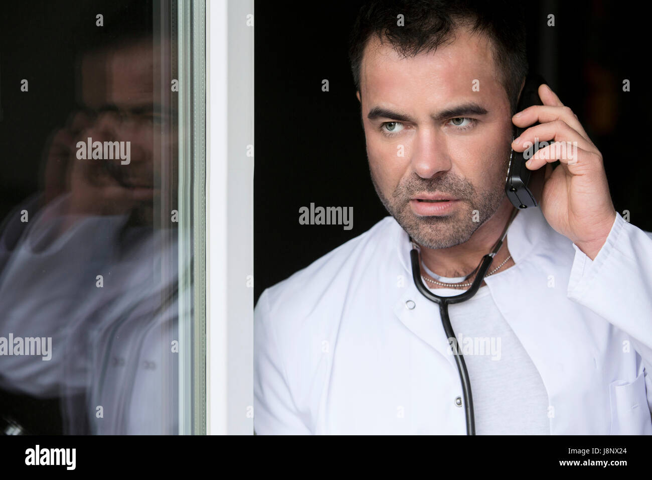 handsome doctor standing by window and talking on the phone Stock Photo ...